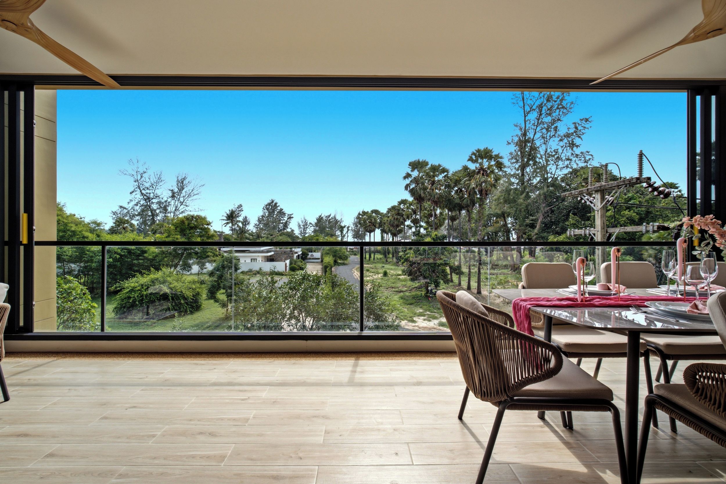 Área de refeições com uma mesa posta para dois, com vista para uma paisagem arborizada e céu limpo.
