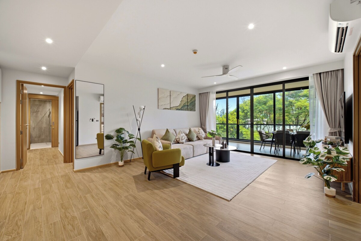 Uma sala de estar ampla, com uma grande janela, um sofá, uma mesa de centro e um espaço para refeições.