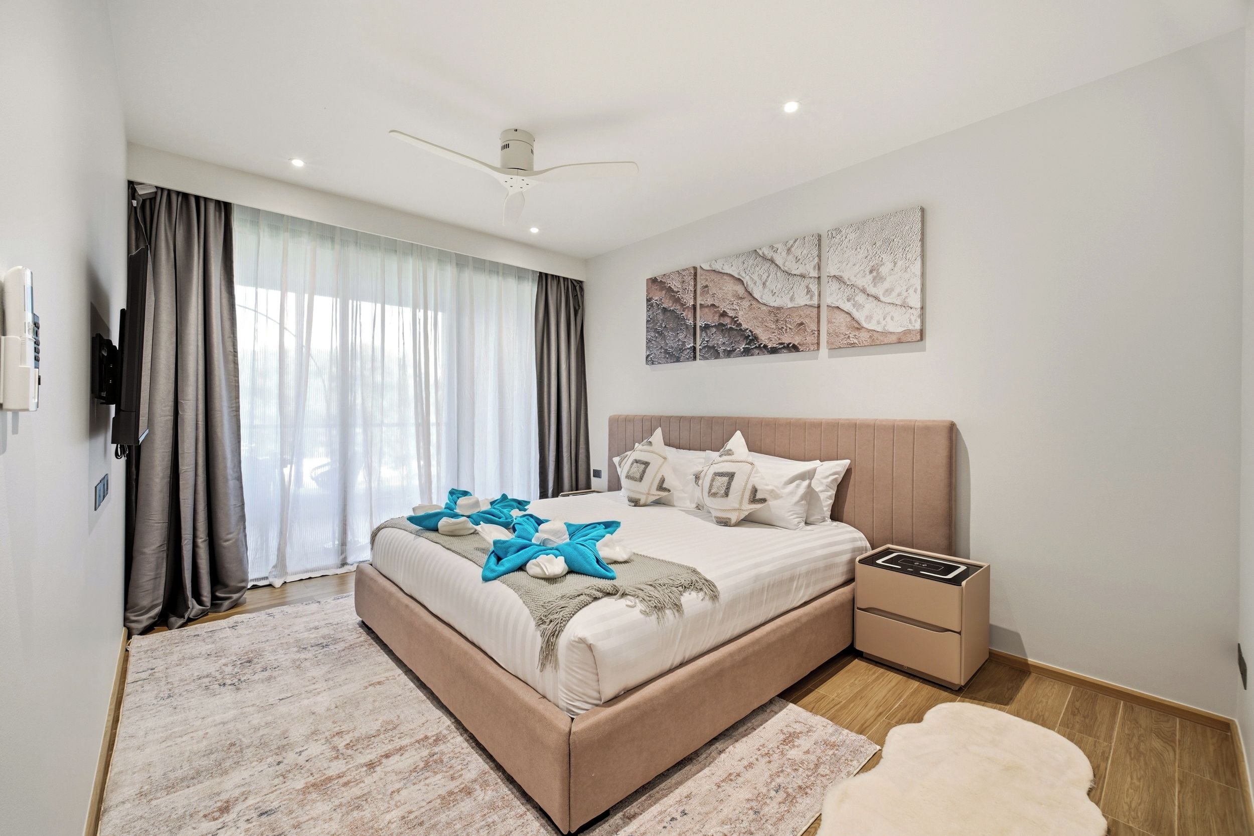 Quarto moderno com uma cama grande, mesa de cabeceira, ventoinha no teto e janela com cortinas.