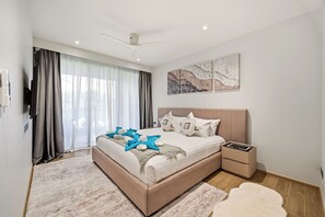 Quarto moderno com uma cama grande, mesa de cabeceira, ventoinha no teto e janela com cortinas.