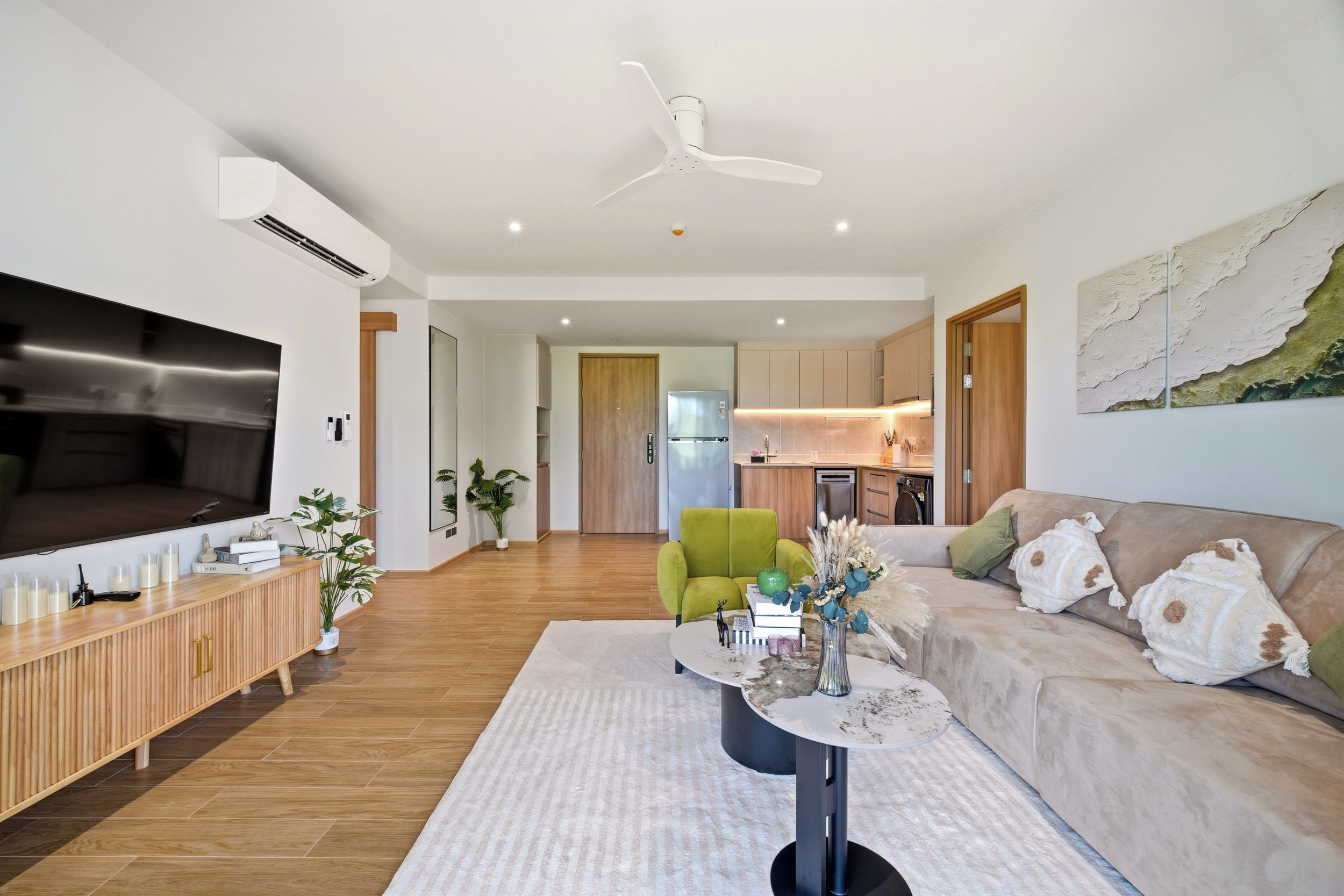 Uma sala de estar moderna com uma TV de tela plana, uma poltrona verde, um sofá bege e um espaço de jantar com armários de madeira.