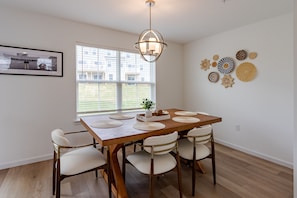 Uma área de refeições com mesa de madeira, cadeiras brancas e luminária pendente.