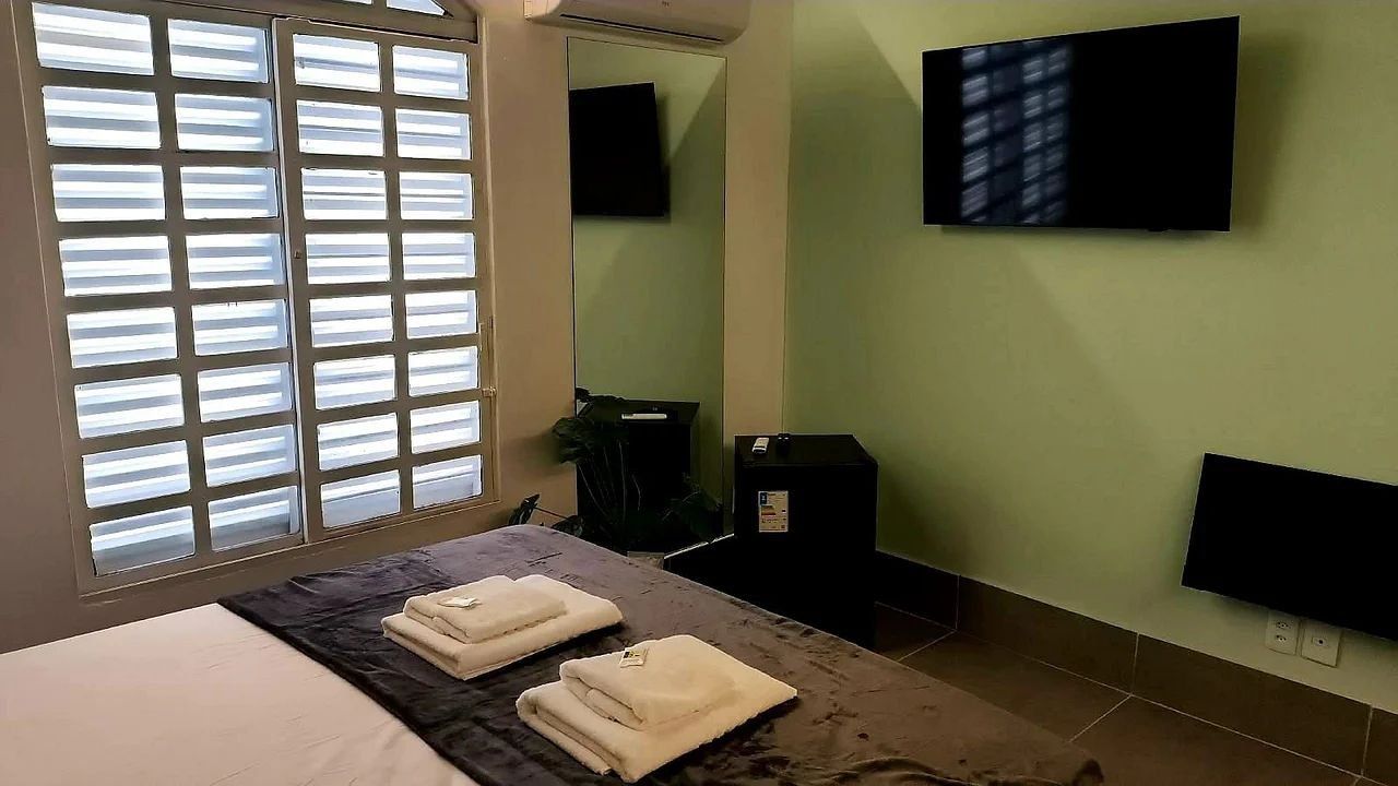 Quarto de hotel com uma cama, televisão fixada na parede e janela com persianas.