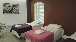 Quarto com duas camas, janela com persianas e obras de arte na parede.