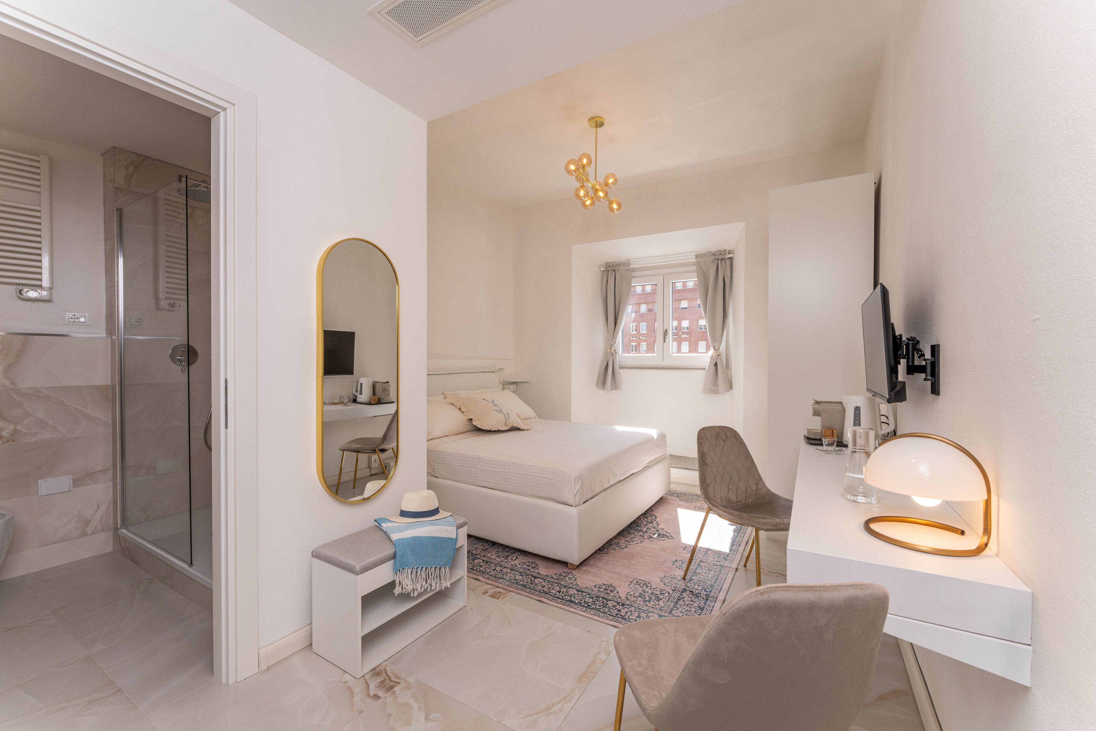 Quarto moderno com cama, escrivaninha, cadeira, espelho e área de chuveiro.
