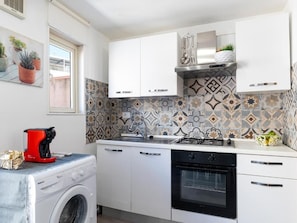 Cozinha compacta com armários brancos, forno embutido, máquina de lavar e cafeteira.