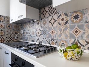 Cozinha com fogão a gás, pia e painel de azulejos decorativo.