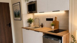 Cozinha moderna com armários brancos, lava-louças de aço inoxidável, micro-ondas e bancada de madeira.