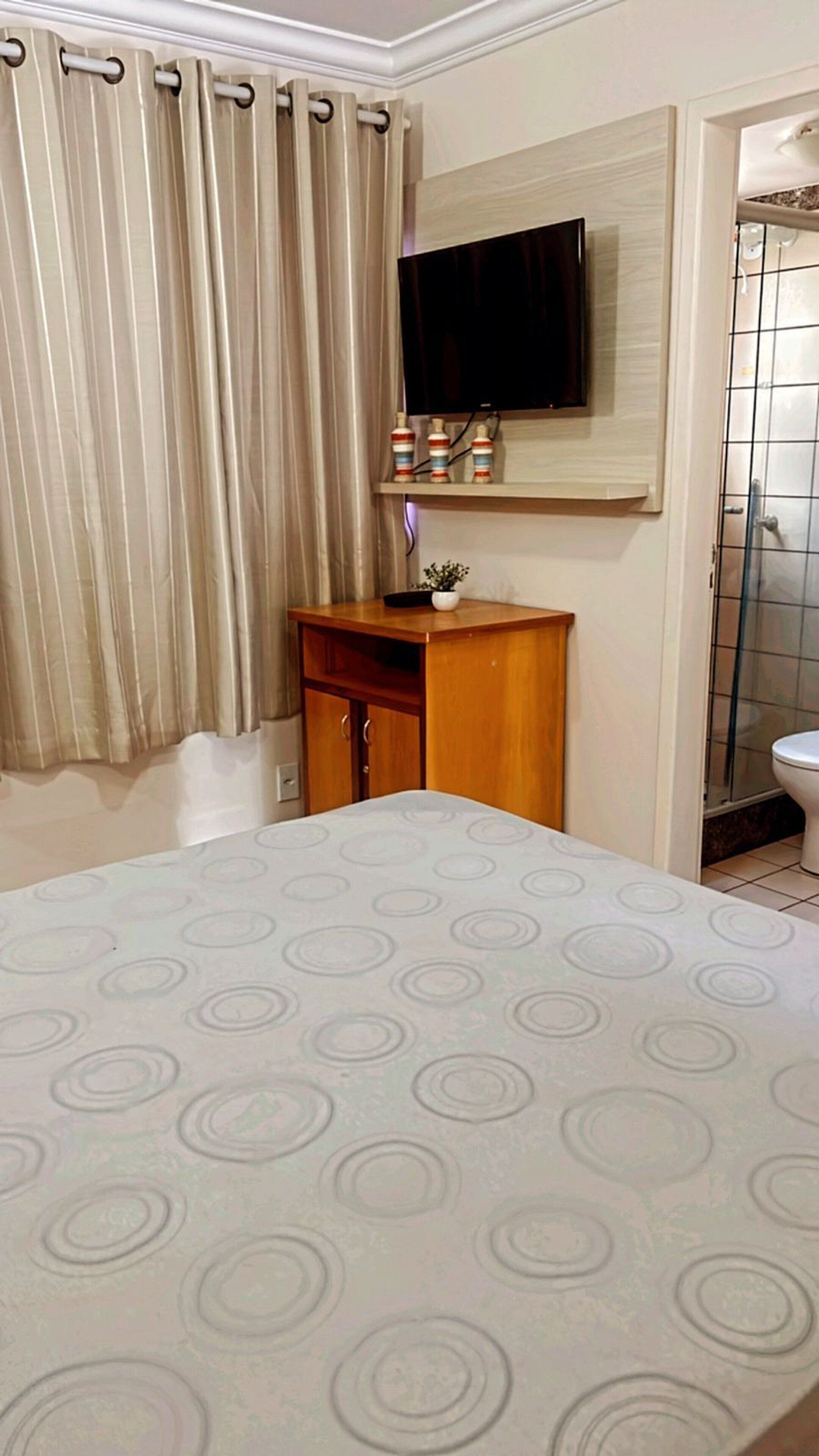 Quarto de hotel com cama, um armário de madeira, televisão fixada na parede e área de chuveiro.