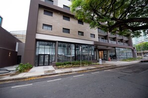 Um edifício moderno com grandes janelas, entrada coberta e uma árvore na frente.