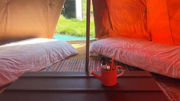 Tenda com duas camas, uma janela e um jarro vermelho para água sobre um tapete.
