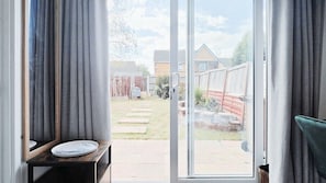 Quarto com porta de vidro deslizante que dá para um quintal com cerca de madeira, um banco e um pequeno jardim.