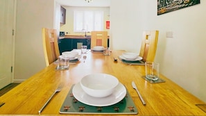 Mesa de jantar posta com pratos, tigelas, copos e talheres, com cadeiras ao redor.