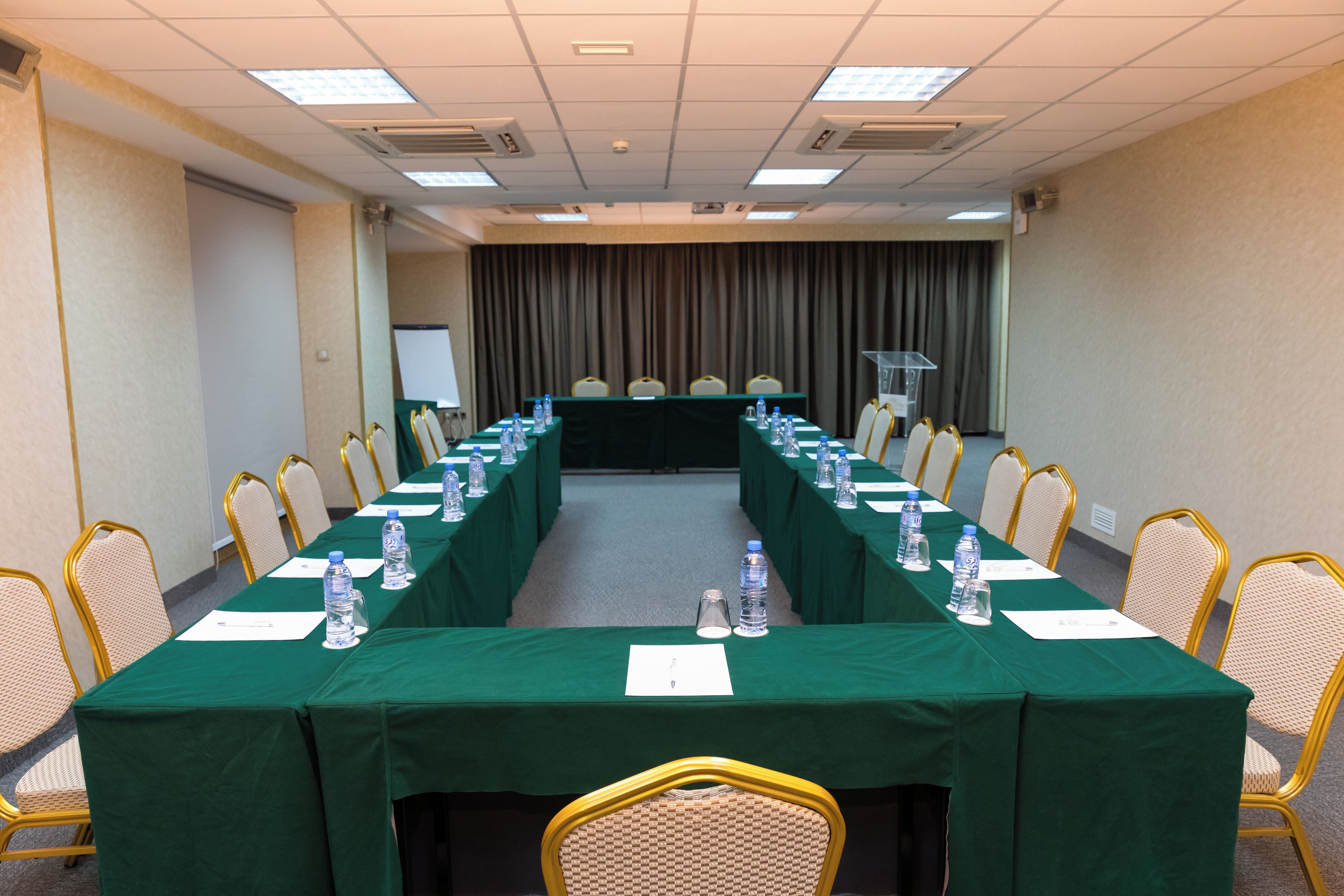 Uma sala de conferências com uma mesa comprida, cadeiras, garrafas de água e uma tela de projetor.