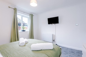 Quarto de hotel com cama, televisão de tela plana na parede, radiador e janela com cortinas.