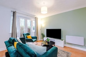 Uma sala de estar moderna com sofás verde-água, uma TV de tela plana e uma janela grande com cortinas.