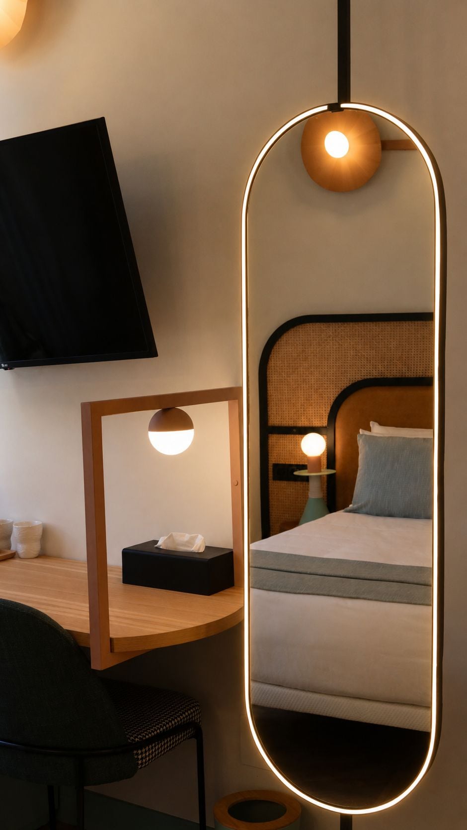 Quarto de hotel com cama, escrivaninha, cadeira e espelho com iluminação.