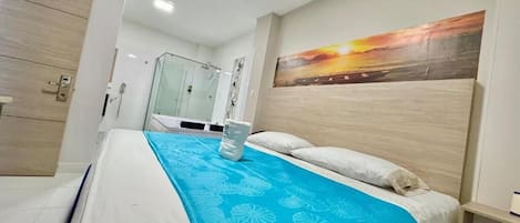 Quarto de hotel com cama, chuveiro, um quadro na parede e toalha sobre a cama.