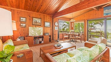 Interior de uma cabana de madeira com sala de estar, área de jantar e varanda com vista.