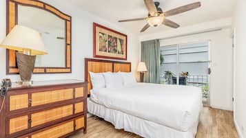 Quarto de hotel com cama, cómoda de madeira, ventoinha no teto, espelho grande e janela com vista.