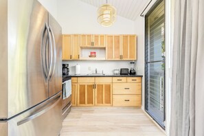Cozinha moderna com armários de madeira, geladeira de aço inoxidável e porta de vidro deslizante para o exterior.