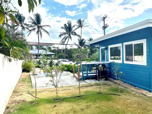 Um imóvel residencial com fachada azul, varanda coberta e pequeno gramado.