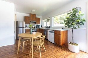 Cozinha moderna com armários de madeira, eletrodomésticos de aço inoxidável, mesa de jantar com cadeiras e um vaso de planta.