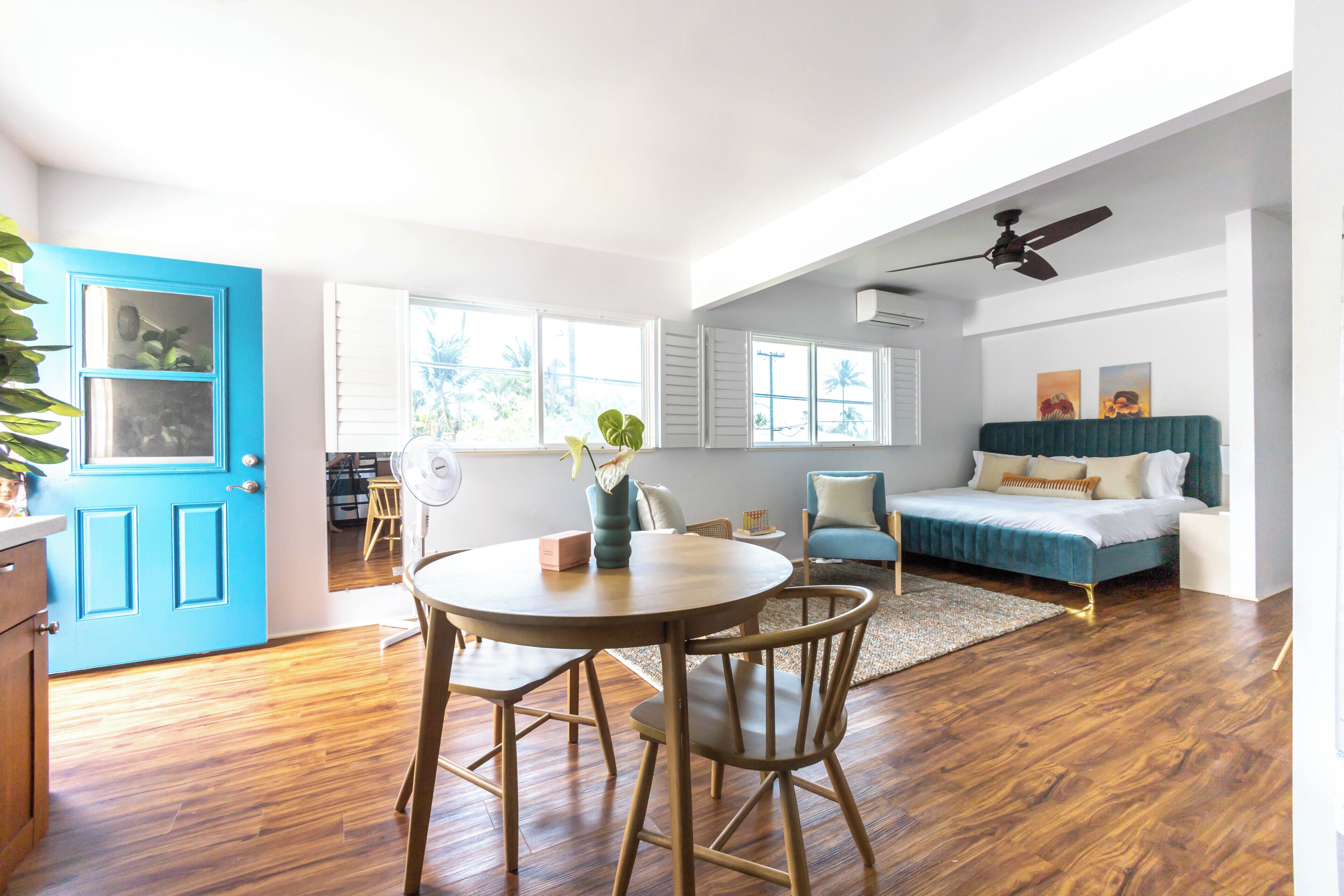 Um quarto amplo com piso de madeira, uma mesa de jantar redonda, um sofá azul e um ventilador de teto.