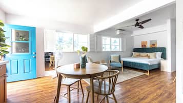 Um quarto amplo com piso de madeira, uma mesa de jantar redonda, um sofá azul e um ventilador de teto.