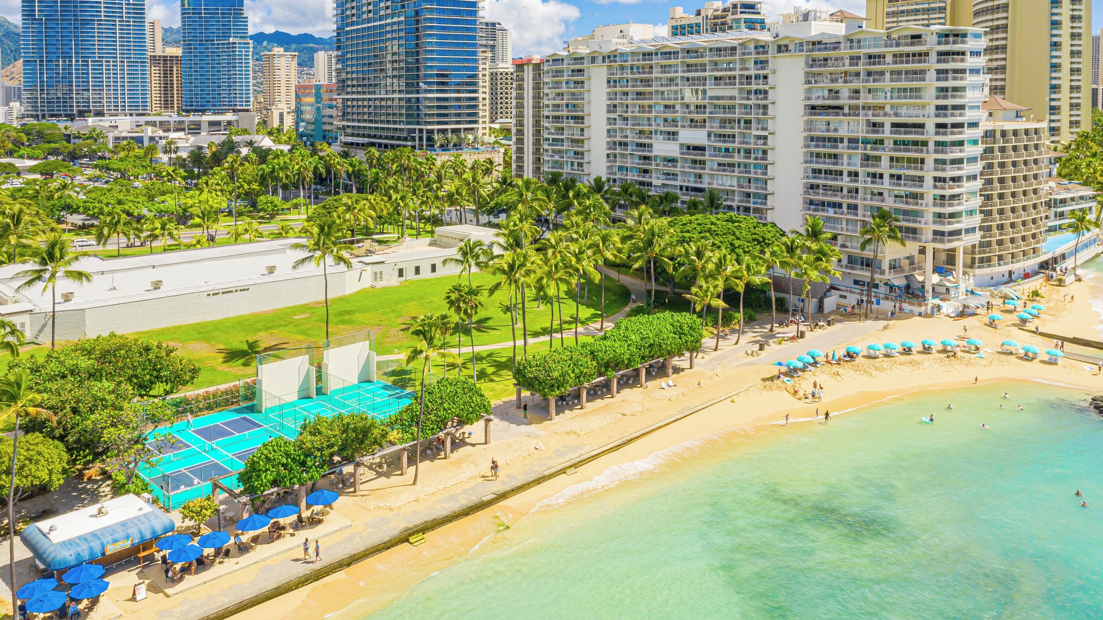 Um hotel na praia com vários edifícios altos, uma área de piscina e uma praia de areia.