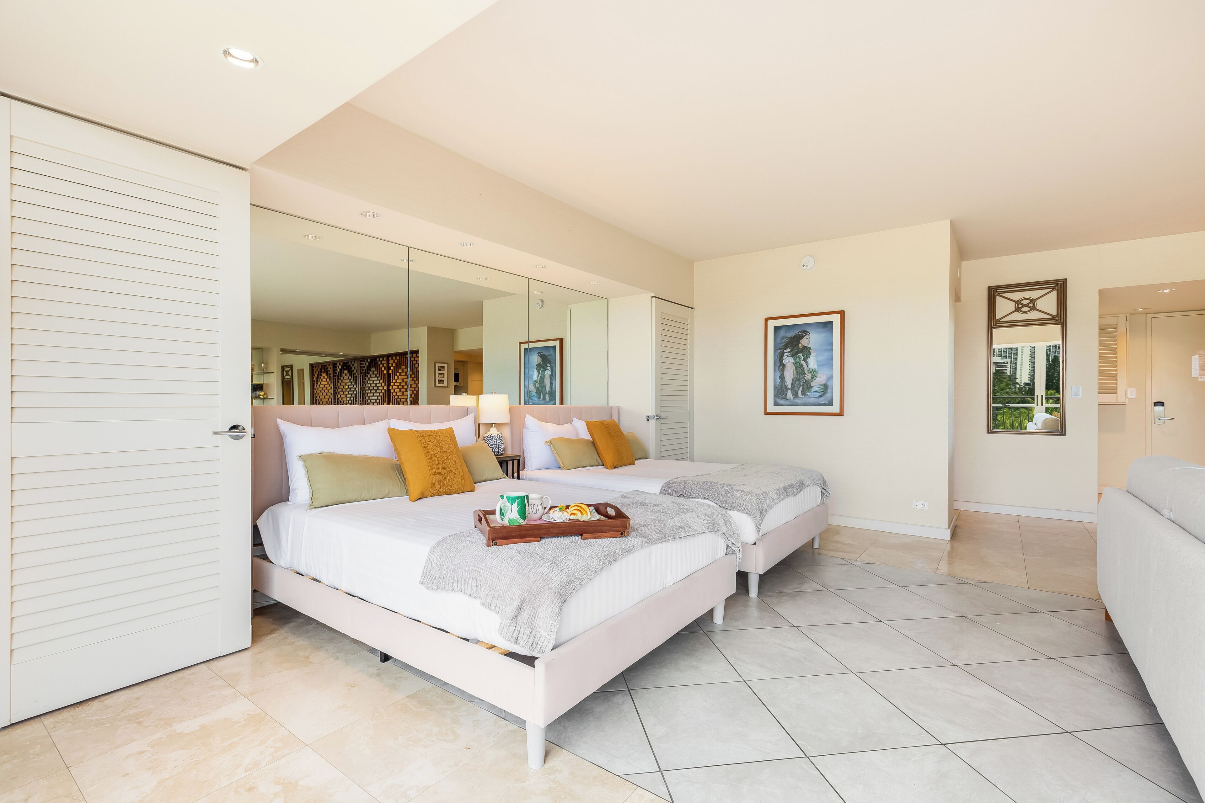 Quarto moderno com duas camas, um espelho grande e um espaço de refeições com uma bandeja de comida.
