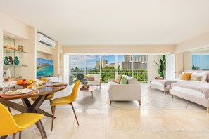 Ampla sala de estar com mesa de jantar, cadeiras amarelas, sofá e varanda com vista para a cidade.