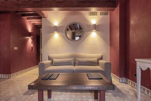 Quarto aconchegante com um sofá estampado, uma mesa de centro de madeira e duas luminárias fixadas na parede.
