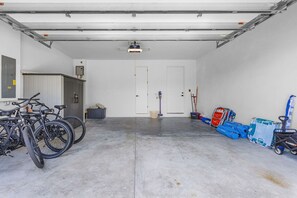 Garagem com duas bicicletas estacionadas à esquerda, uma cesta de roupa e materiais de limpeza à direita.