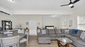 Uma sala de estar moderna com um sofá seccional, uma mesa de centro de vidro e uma área de jantar com ilha de cozinha.