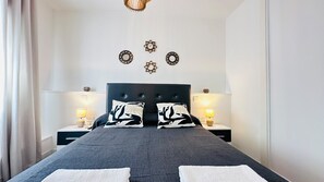 Quarto de hotel com uma cama grande, duas luminárias de cabeceira e espelhos decorativos na parede.