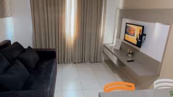 Sala de estar com sofá escuro, TV em um móvel e cortina.