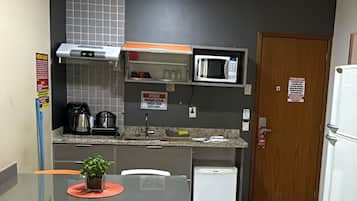 Cozinha compacta com micro-ondas, chaleira e cafeteira. Há uma pequena mesa com uma planta.
