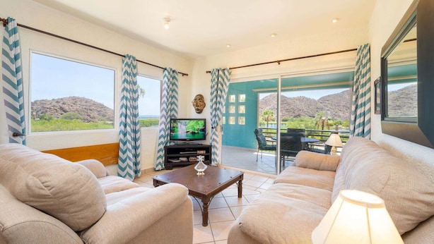 Sala de estar com televisão, sofá e vista para uma paisagem montanhosa através de uma porta de vidro deslizante.