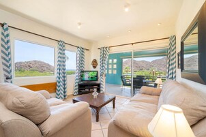 Sala de estar com televisão, sofá e vista para uma paisagem montanhosa através de uma porta de vidro deslizante.