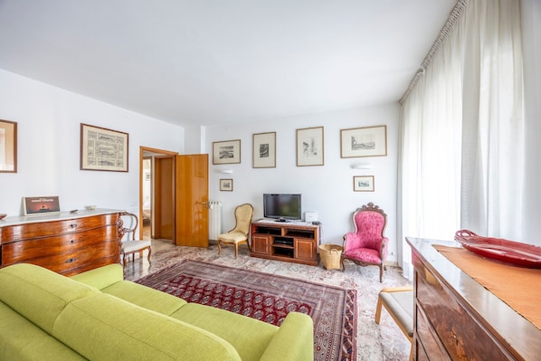 Uma sala de estar com um sofá verde, móveis de madeira, uma televisão e quadros nas paredes.