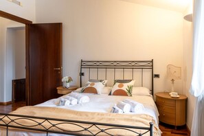 Cama bem arrumada com travesseiros e toalhas, mesa de cabeceira com abajur e guarda-roupa de madeira.