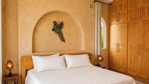 Quarto com cama grande, guarda-roupa de madeira e cabeceira decorativa.