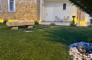 Um gramado bem cuidado com um banco de pedra e uma área de pátio com móveis de exterior.
