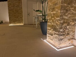 Uma área externa moderna com uma parede de pedra, um vaso de planta e uma cadeira de metal.