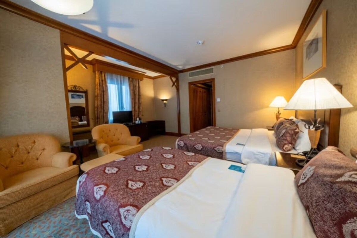 Quarto de hotel com duas camas, um sofá, uma escrivaninha e uma televisão.