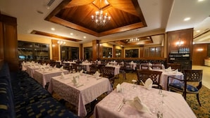 Restaurante com várias mesas preparadas para refeições, apresentando decoração clássica com painéis de madeira e lustres.
