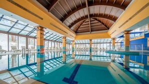 Uma piscina interna com paredes de vidro transparente, piso ladrilhado e teto de madeira.
