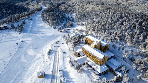 Uma cabana coberta de neve com uma pista de esqui ao fundo.