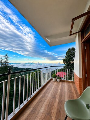 Uma varanda com piso de madeira, guarda-corpo branco e vista para uma paisagem montanhosa.